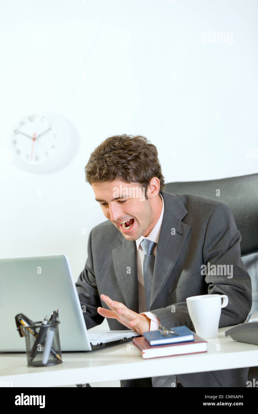 Shocked modern businessman sitting at office desk and discontentedly ...
