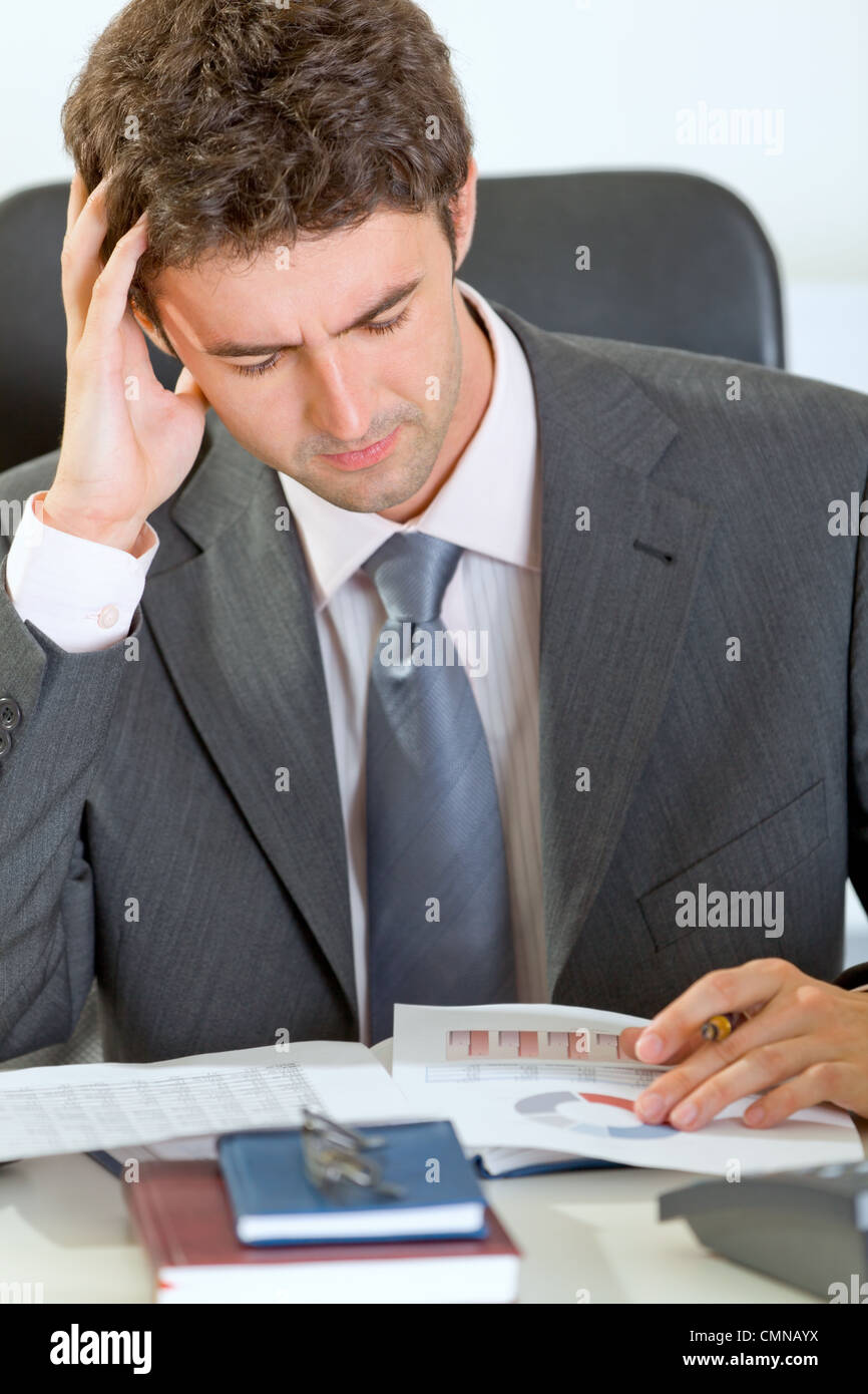 Stressed modern businessman sitting at office desk and working with ...