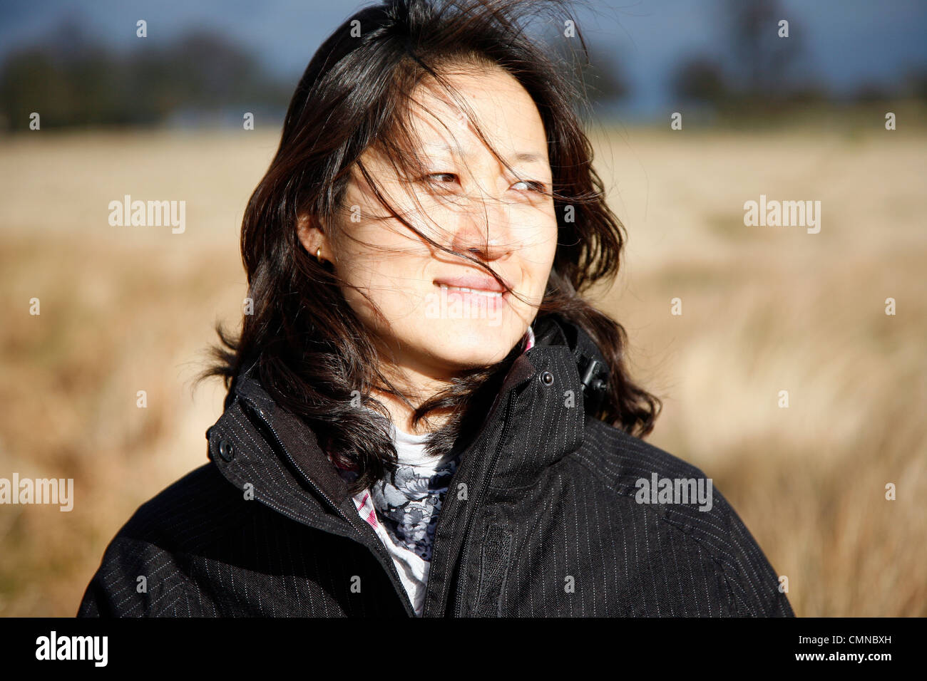 Portrait smiling asian woman, looking off into distance in the field ...
