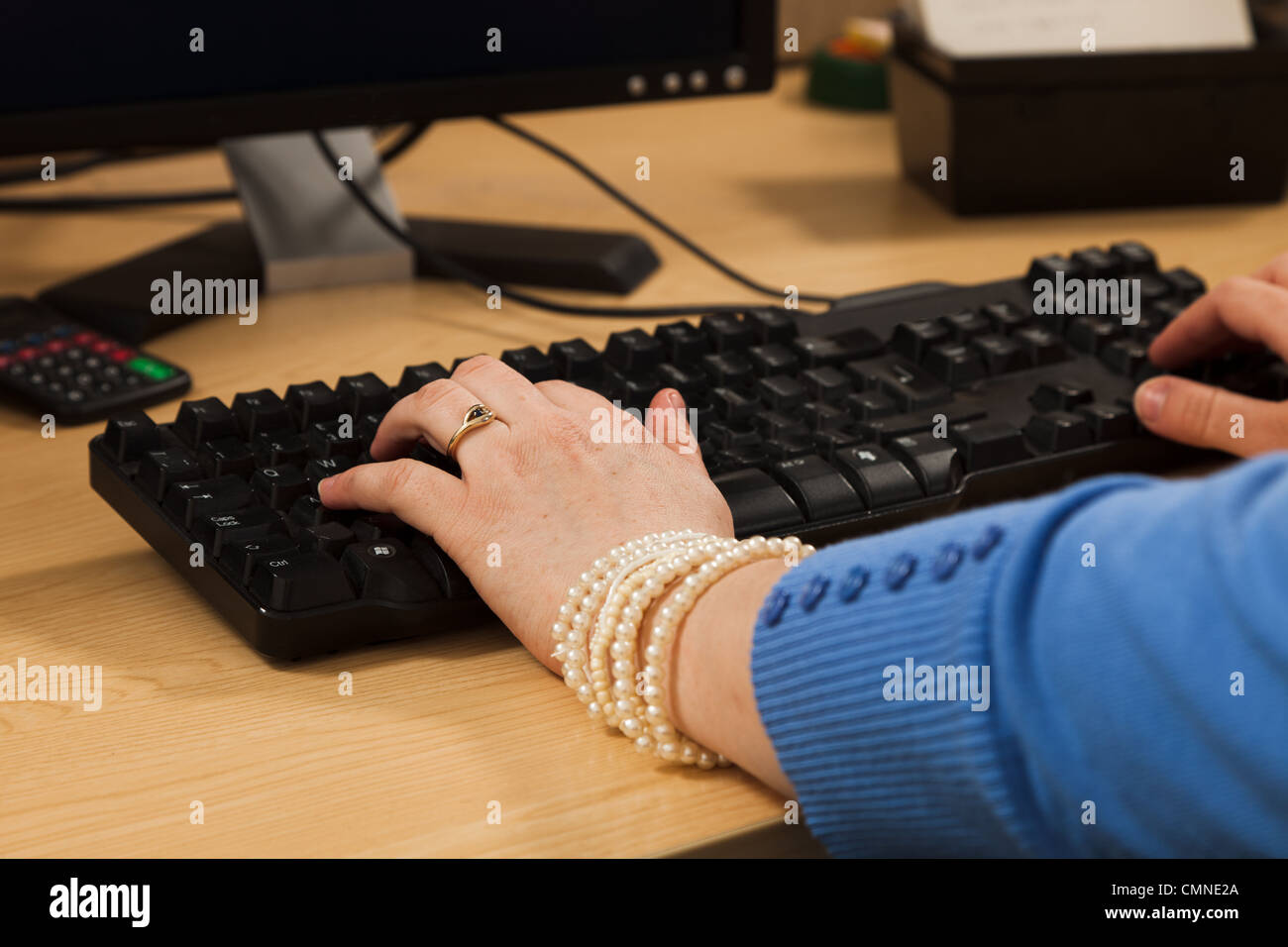 A female office worker at a computer keyboard typing. Shot also shows ...
