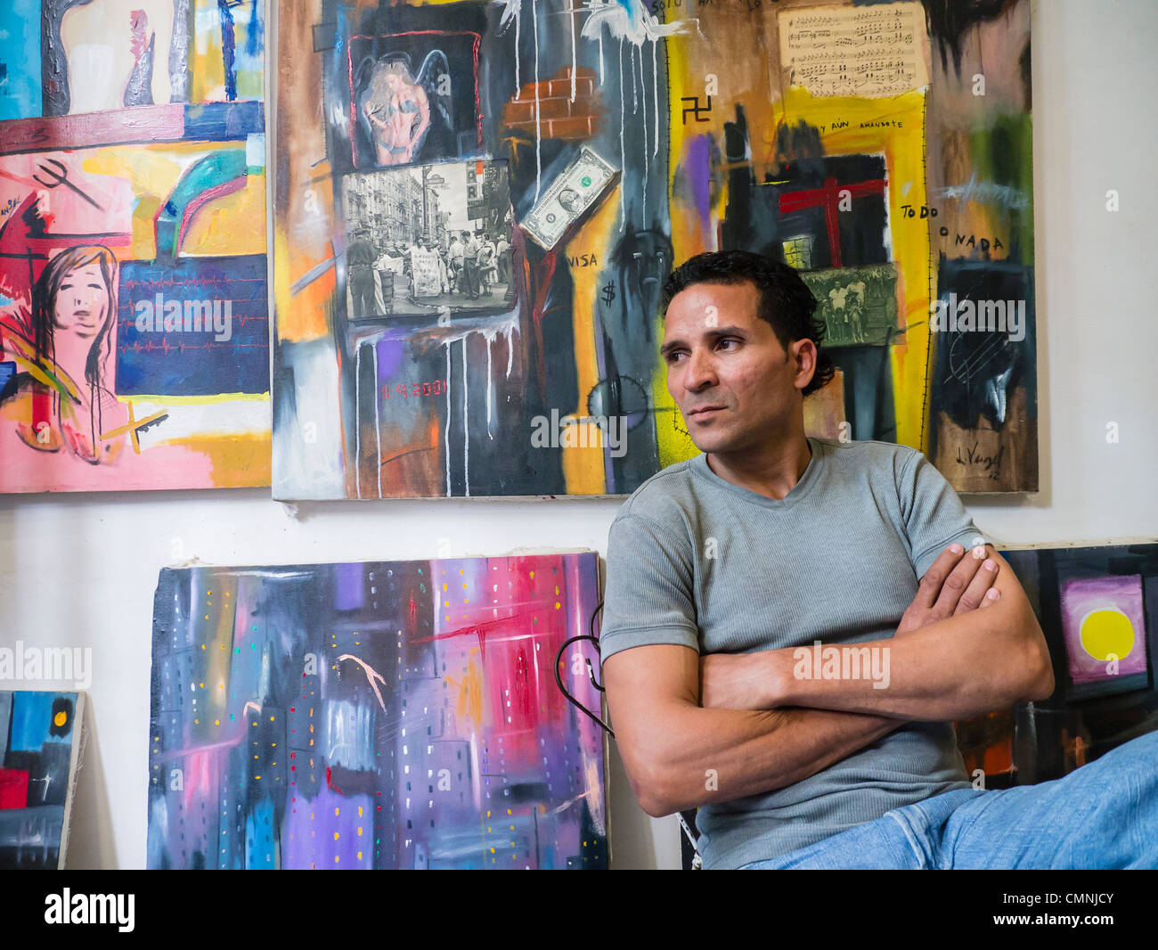 A Cuban male artist sits in his studio with his paintings on display on ...