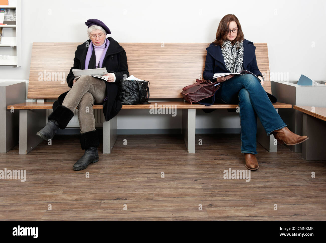 Two women, sitting in mirrored poses, in the waiting room of a general ...