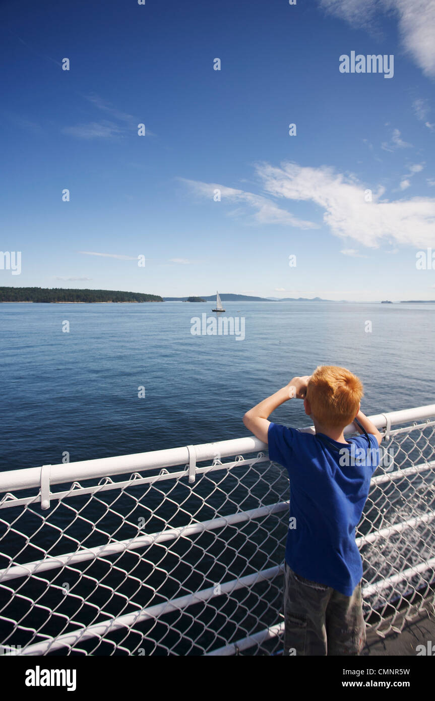 A young boy looks over the ocean with binoculars, from a deck of a ...