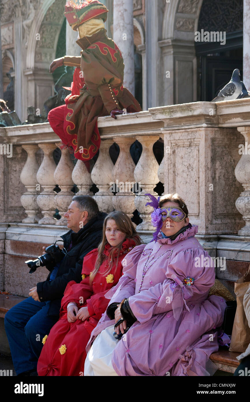 Family in carnival costume sit on a bench looking bored as a carnival ...