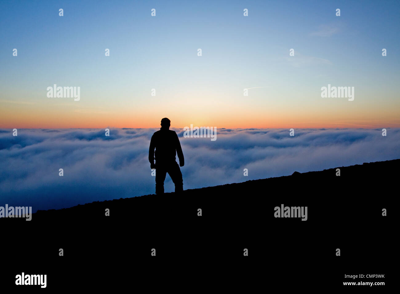 Silhouette of a man at sunset above a cloud inversion on the mountain ...