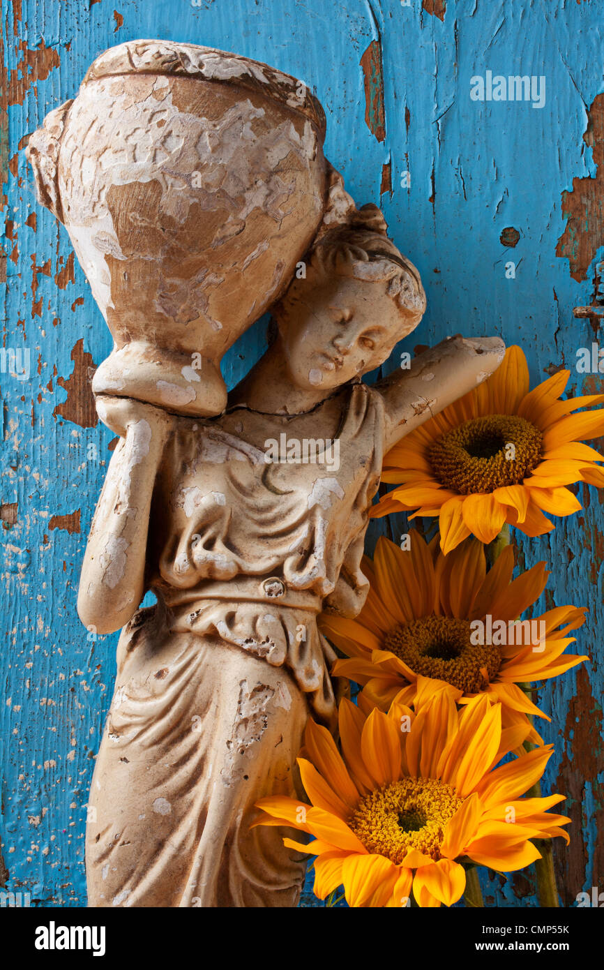 Broken statue of woman with sunflowers leaning against worn blue wall ...