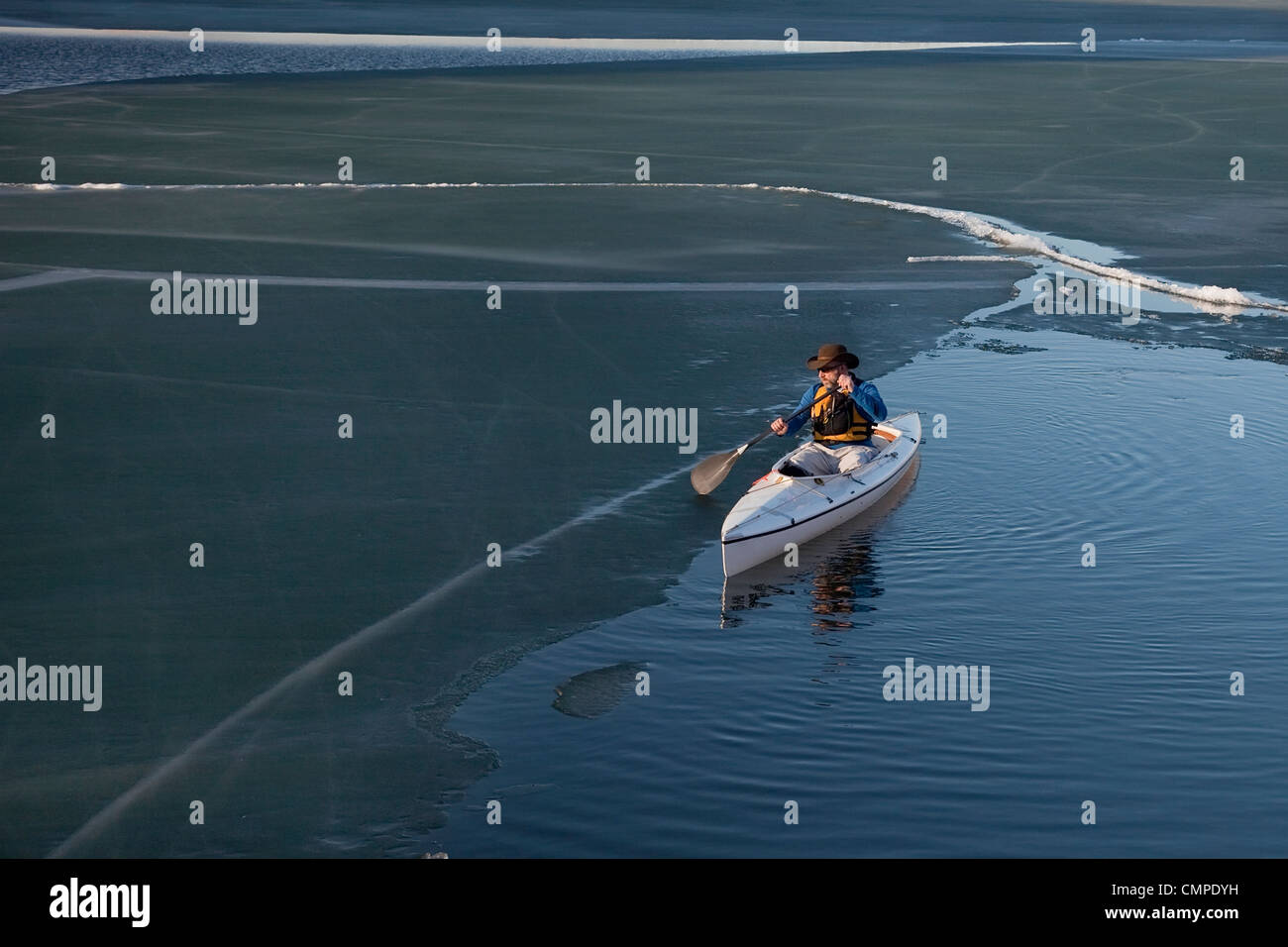 paddling decked expedition canoe on a lake covered with dark soft ice ...