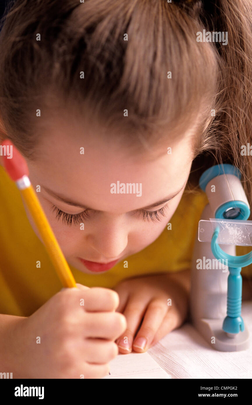 Young girl writing at school studying with microscope Stock Photo - Alamy
