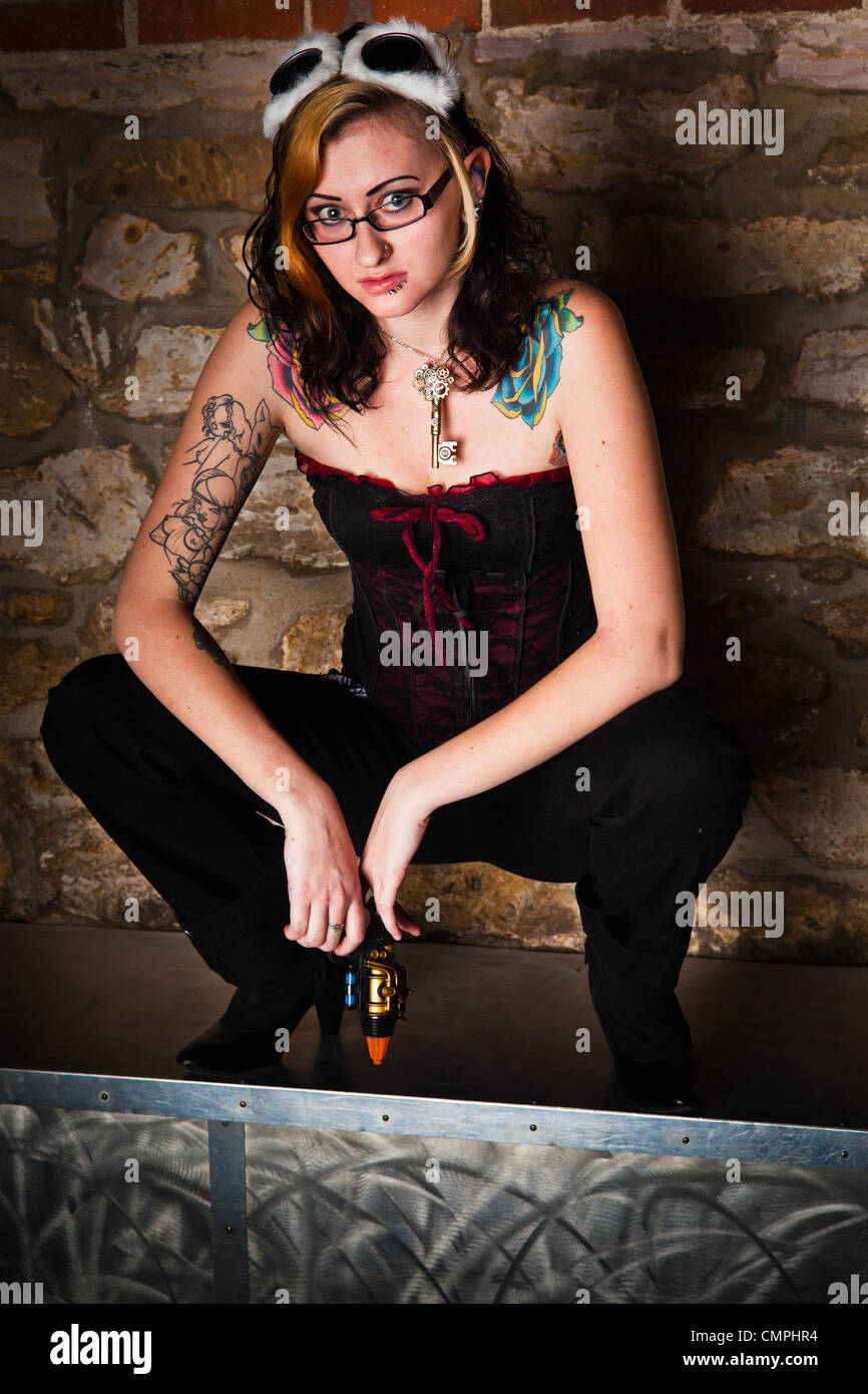 A brunette woman dressed in steampunk themed attire poses with goggles ...
