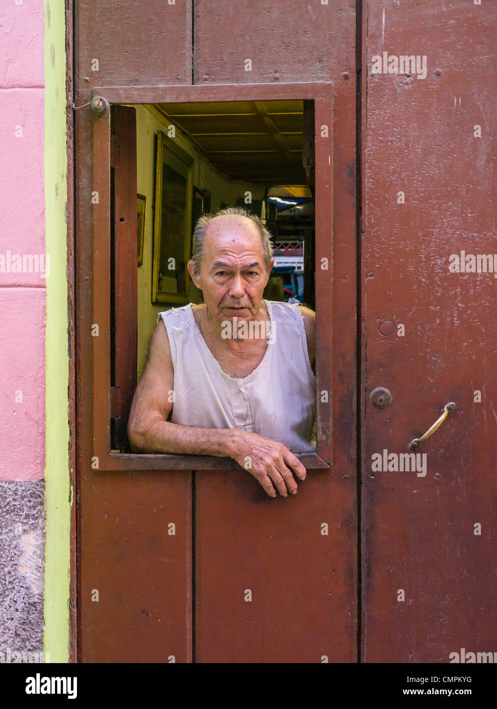 An elderly Cuban man leans outside of the opening in his front door in ...