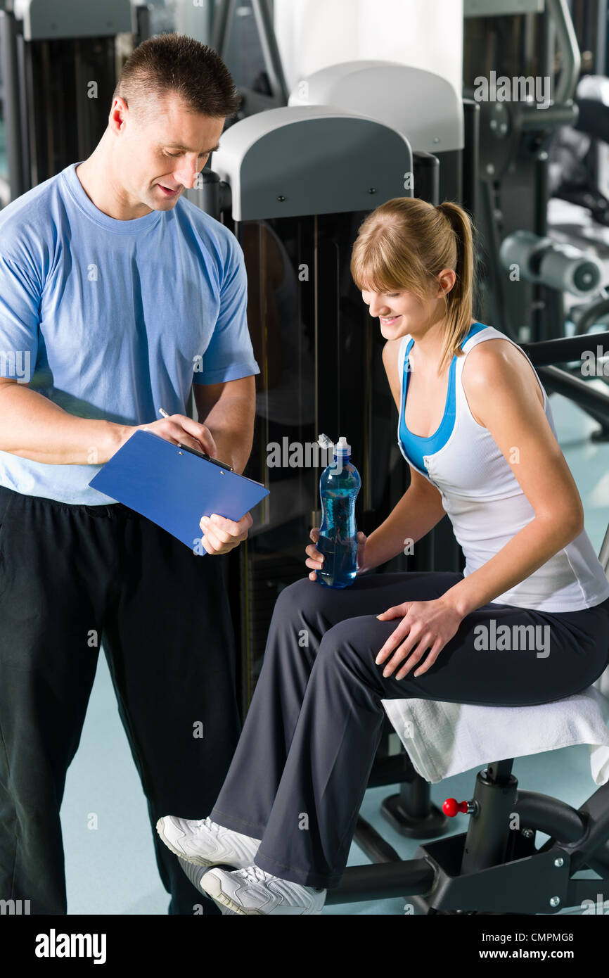 Young woman with personal trainer look at exercise chart at gym Stock ...