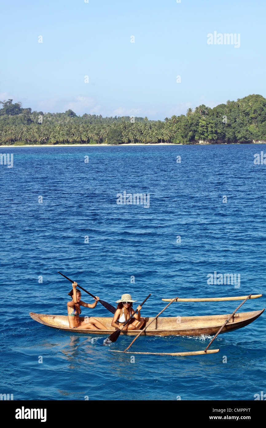 Young women paddling outrigger dugout canoe. Simakakang, Mentawai ...