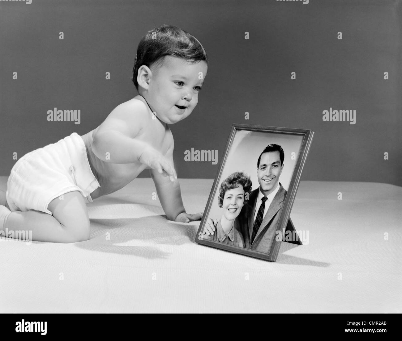 1960s BABY IN DIAPER CRAWLING TO FRAMED PICTURE OF MOTHER AND FATHER ...
