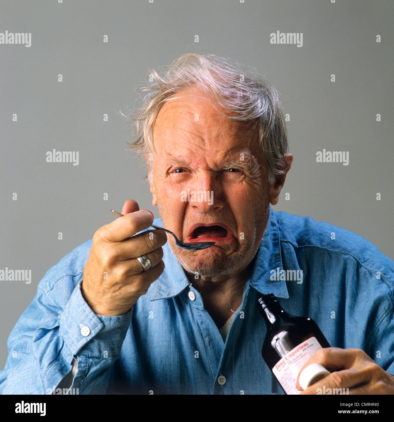 1970s SENIOR MAN TAKING SPOONFUL OF MEDICINE WITH BAD TASTE LOOKING AT ...