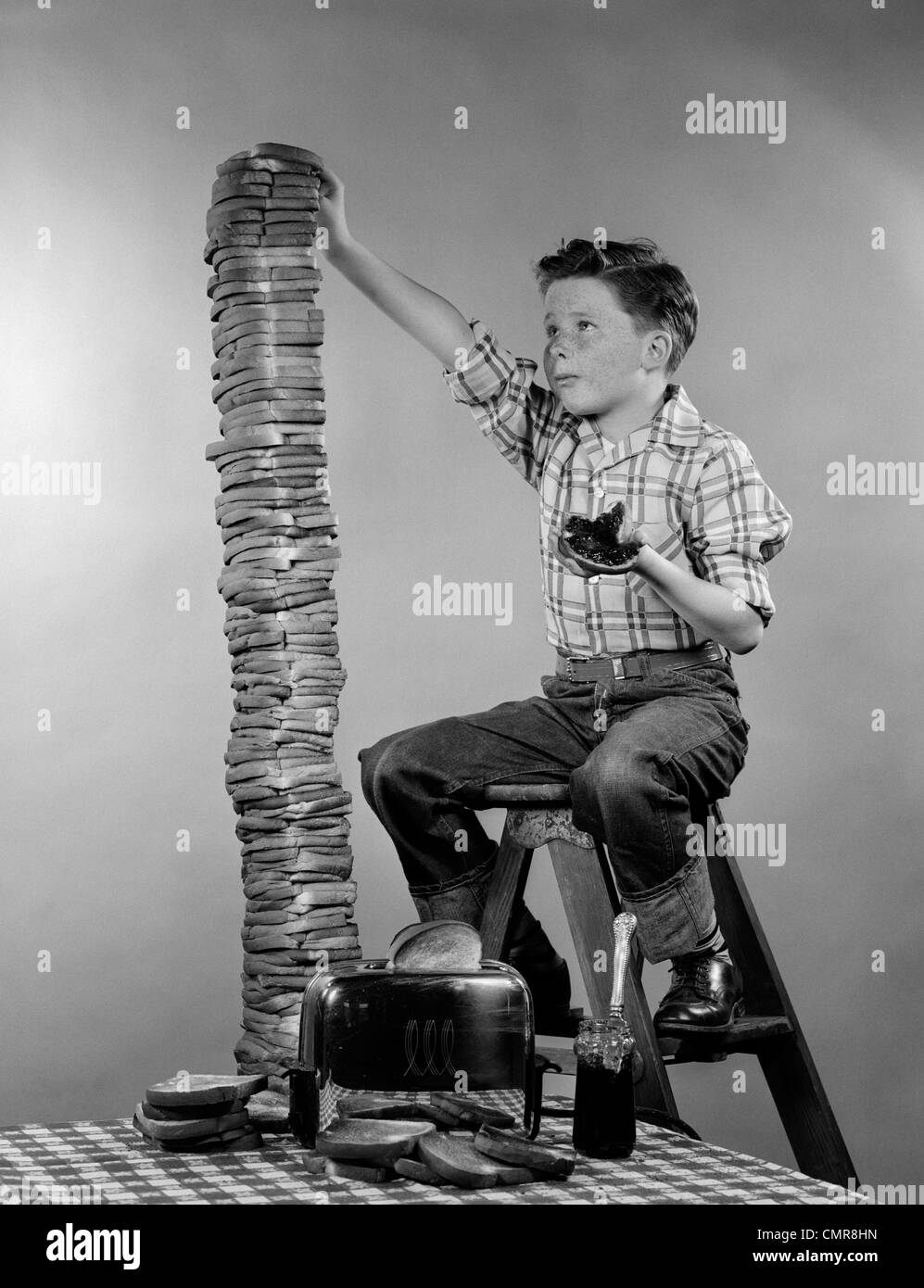 1950s BOY EATING JELLY TOAST SITTING ON LADDER STACKING UP TALL PILE OF ...