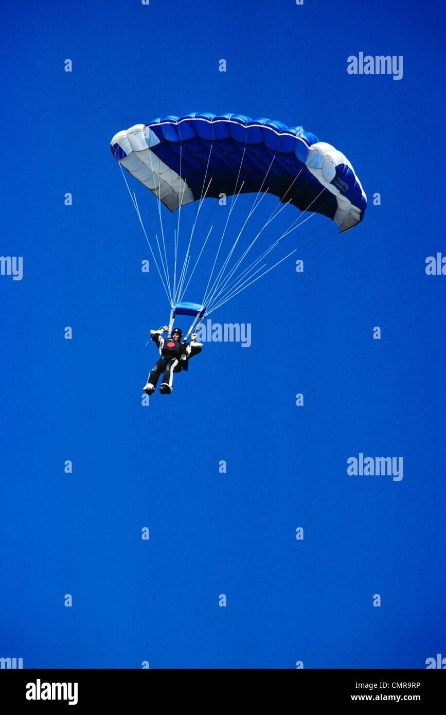1990s SKYDIVER WITH OPEN BLUE AND WHITE PARACHUTE IN BLUE CLOUDLESS SKY ...