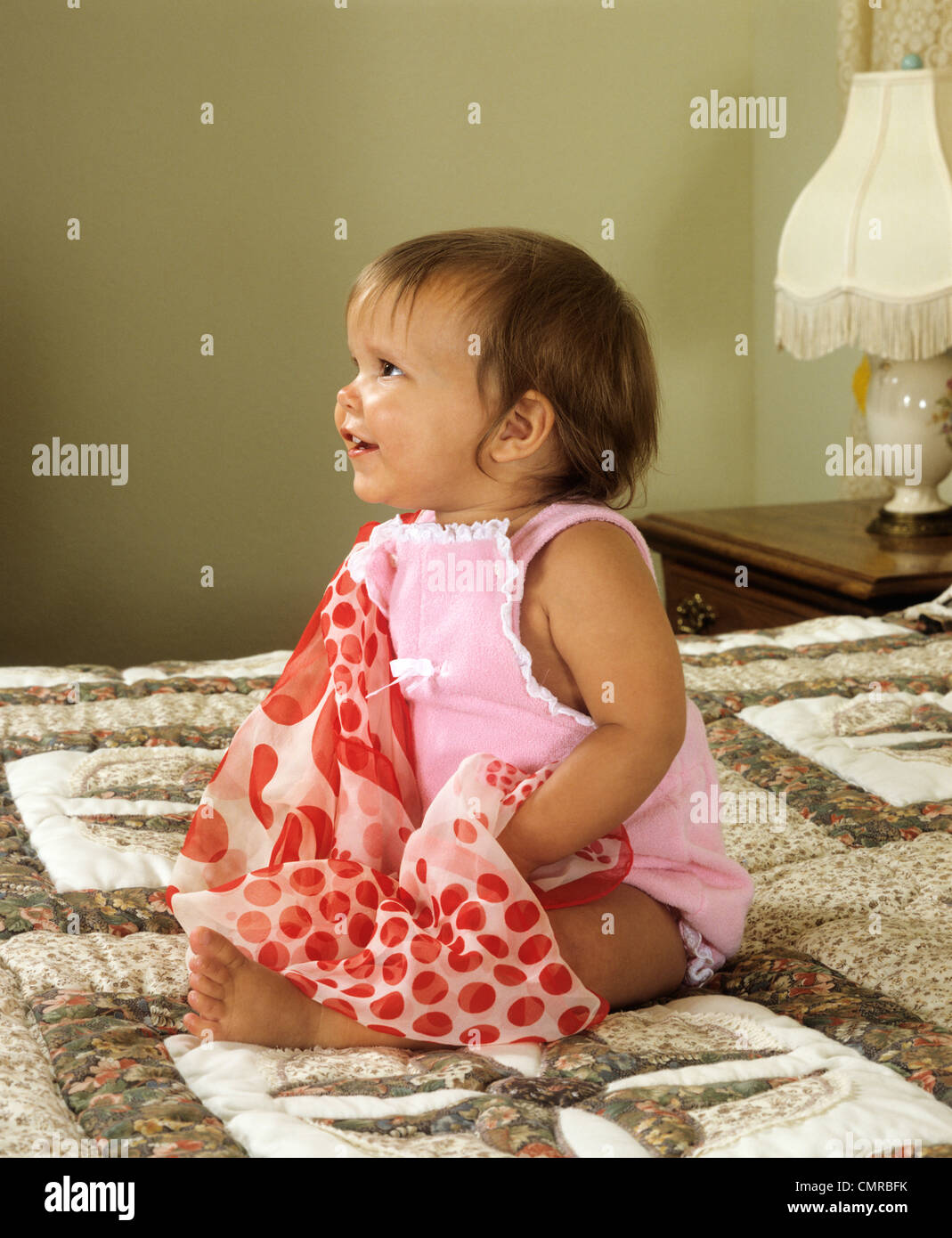 1980s BABY GIRL WEARING PINK SMILING SITTING ON QUILT Stock Photo - Alamy