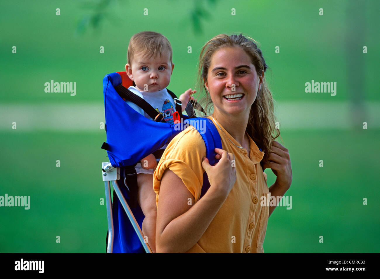 1990s MOTHER CARRYING CHILD IN INFANT CARRIER ON HER BACK LOOKING AT ...