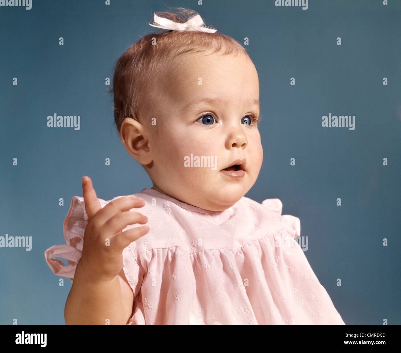 1960s BABY GIRL WEARING PINK DRESS WITH A BOW IN HER HAIR POINTING A ...