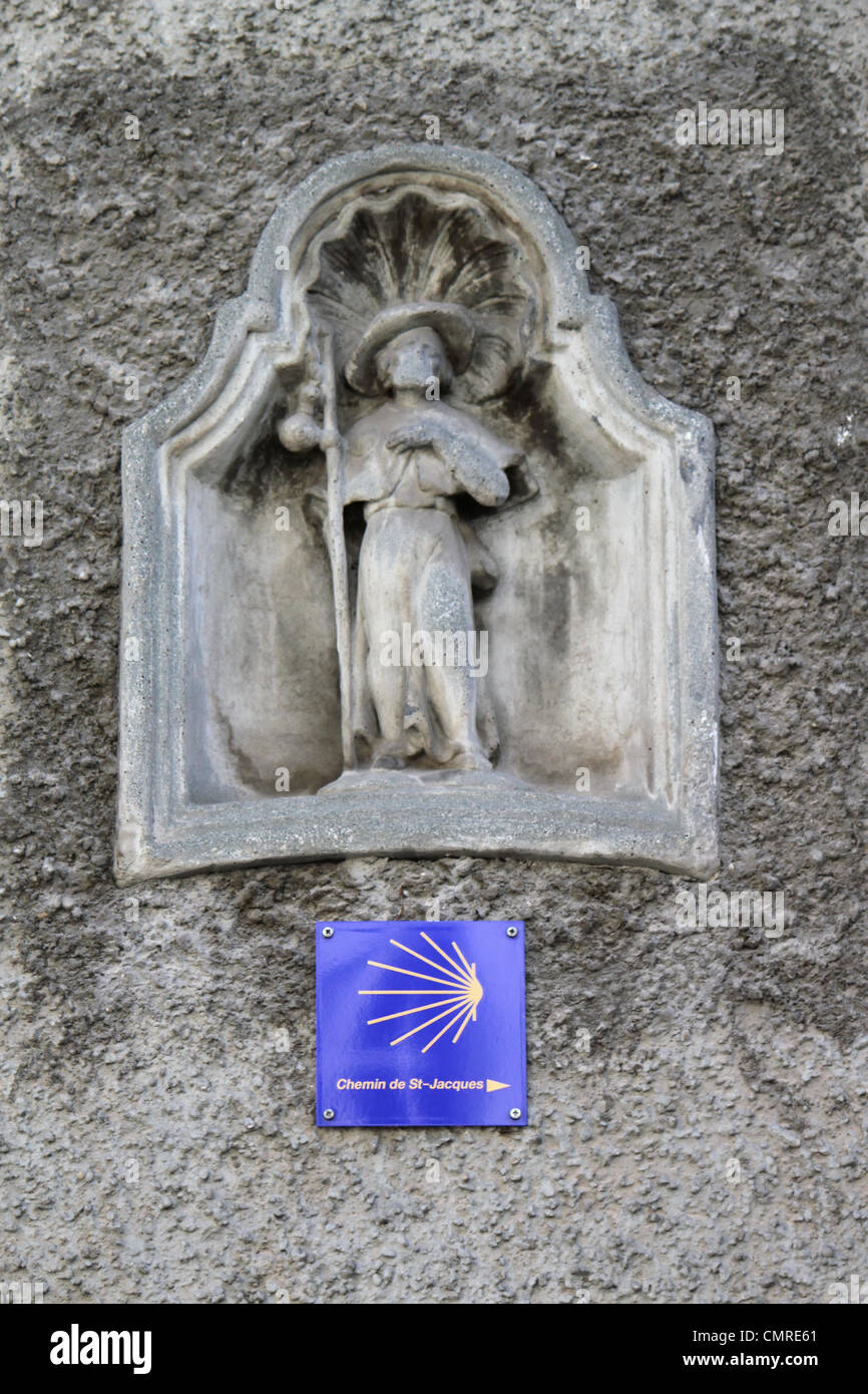 Yellow and blue sign for Compostela way under a pilgrim sculpture on a ...