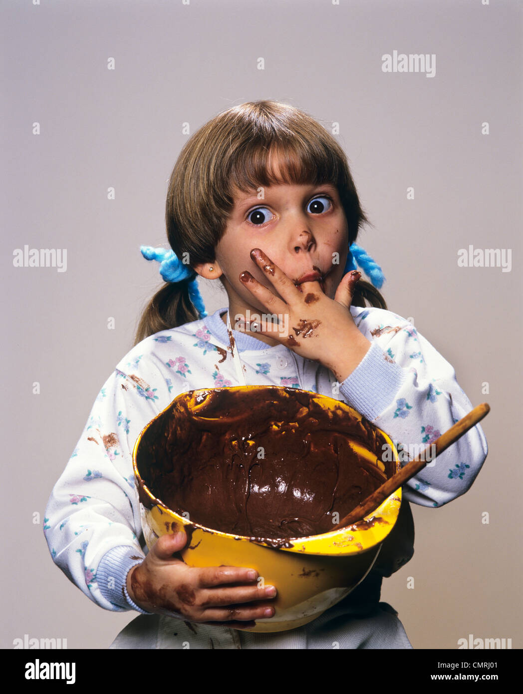 1980s 1990s LITTLE GIRL EATING CHOCOLATE ICING FROM BOWL LOOKING AT ...