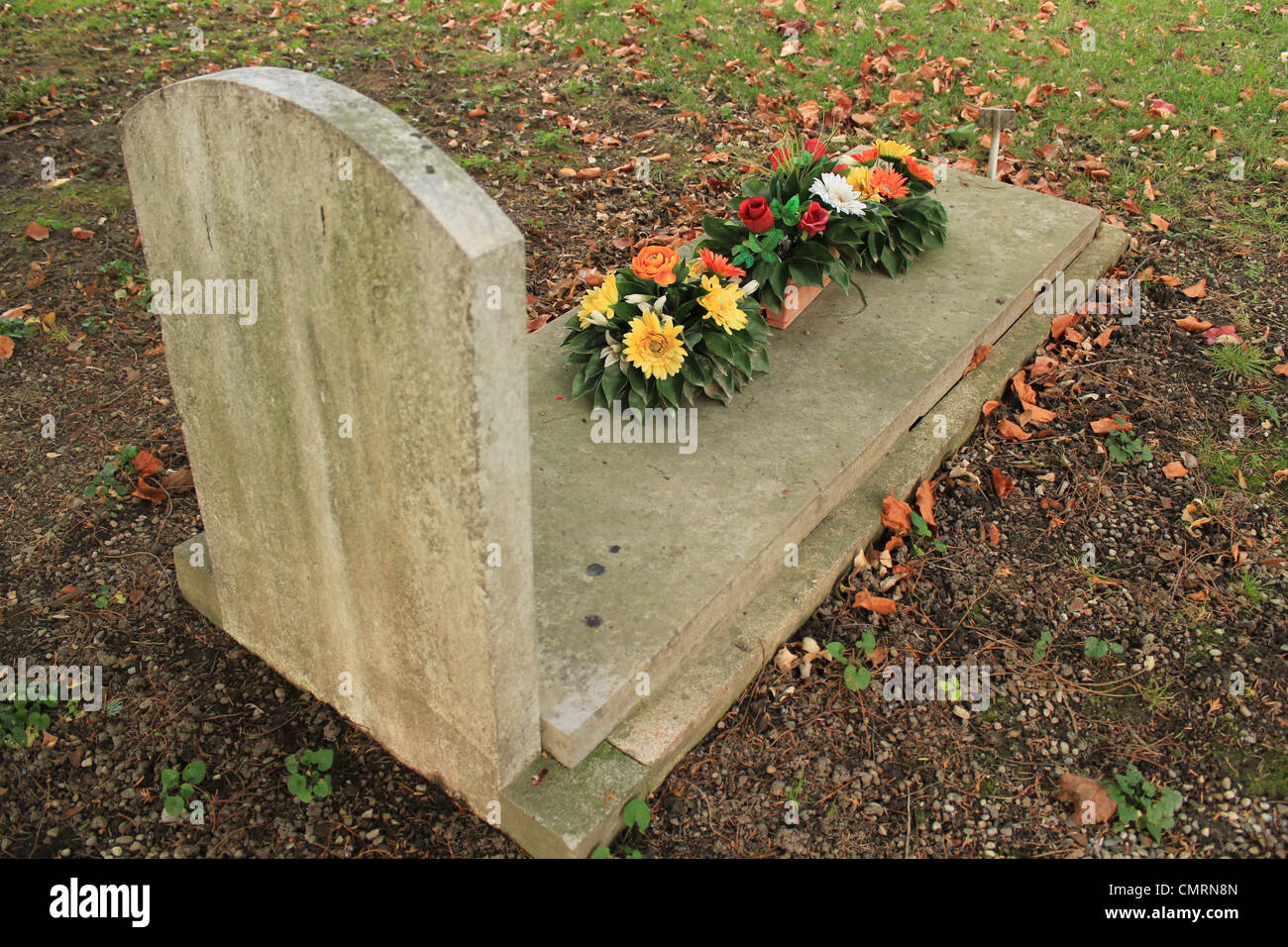Tomb covered with colored flowers with autumn colored red leaves in a ...