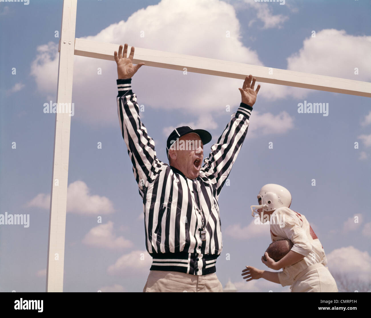 1960s FOOTBALL REFEREE HOLDING UP ARMS AT GOAL POST AS PLAYER MAKES ...