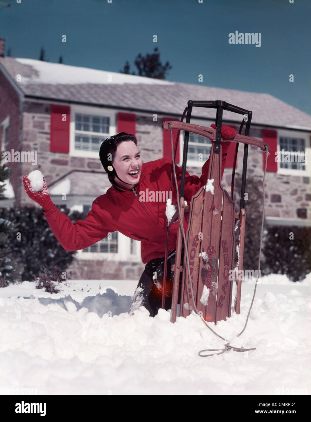 1950s WOMAN HIDING BEHIND SLED THROWING SNOWBALL FRONT STONE HOUSE ...
