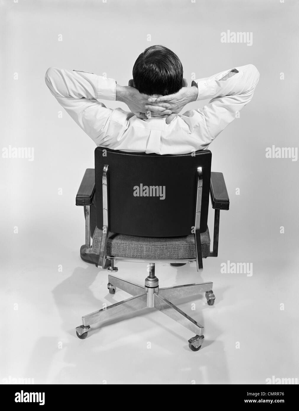 1960s MAN FROM BEHIND SITTING IN OFFICE EXECUTIVE CHAIR HANDS CLASPED ...