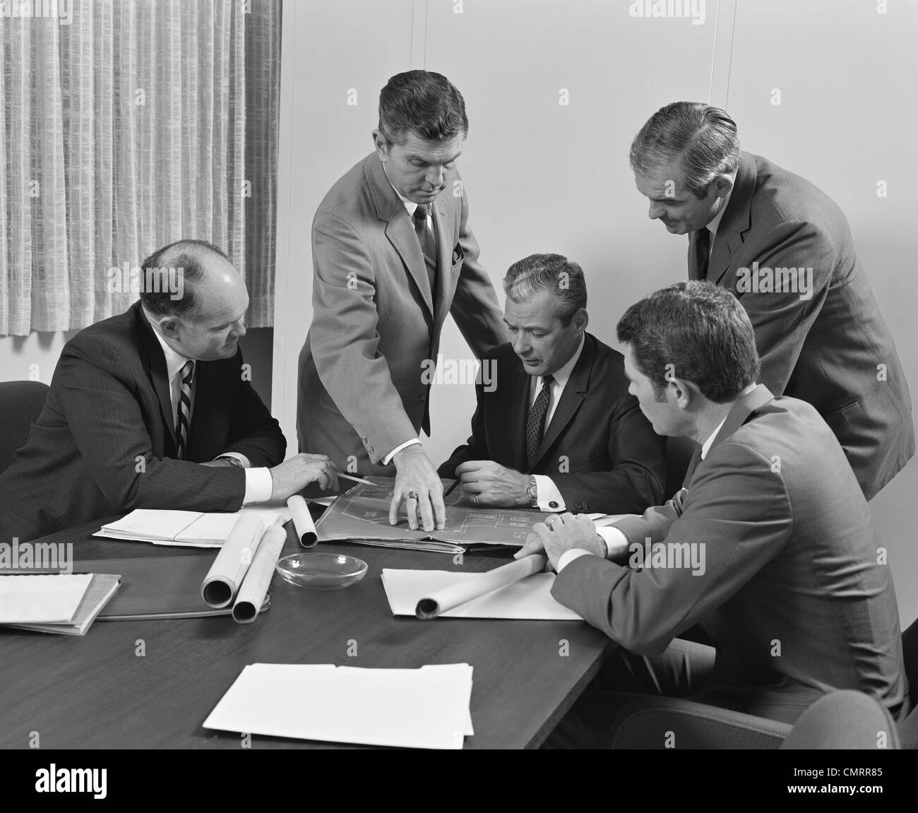 1960s 5 EXECUTIVE BUSINESSMEN AT CONFERENCE TABLE MEETING LOOKING OVER ...