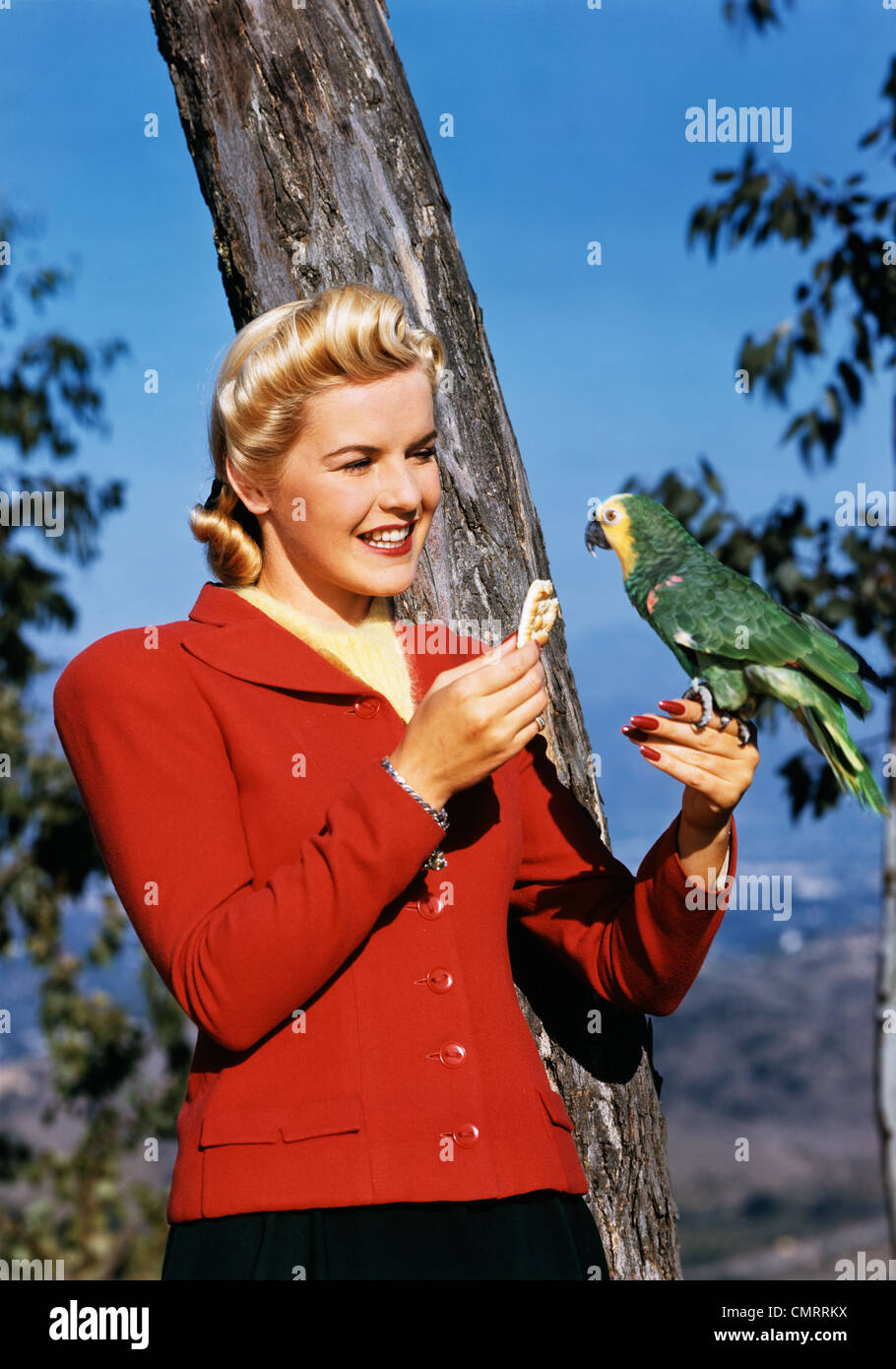 1940s SMILING BLOND WOMAN FEEDING CRACKER TO PARROT OUTDOORS Stock ...