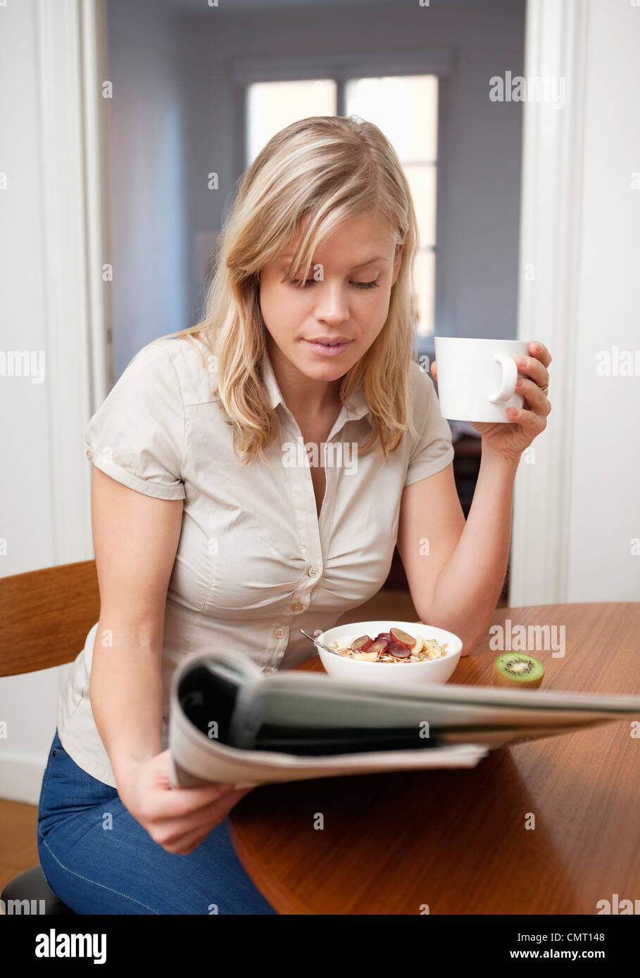 Woman sitting by table reading paper Stock Photo - Alamy