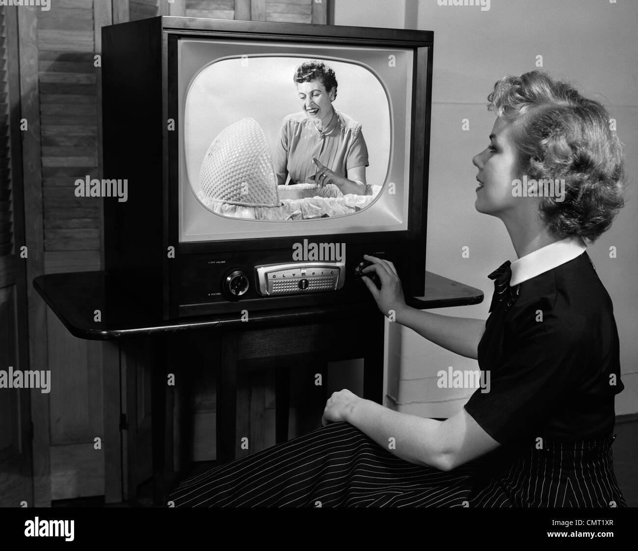 1950s BLONDE WOMAN TURNING DIAL ON TV SET WATCHING PROGRAM ABOUT BABY ...