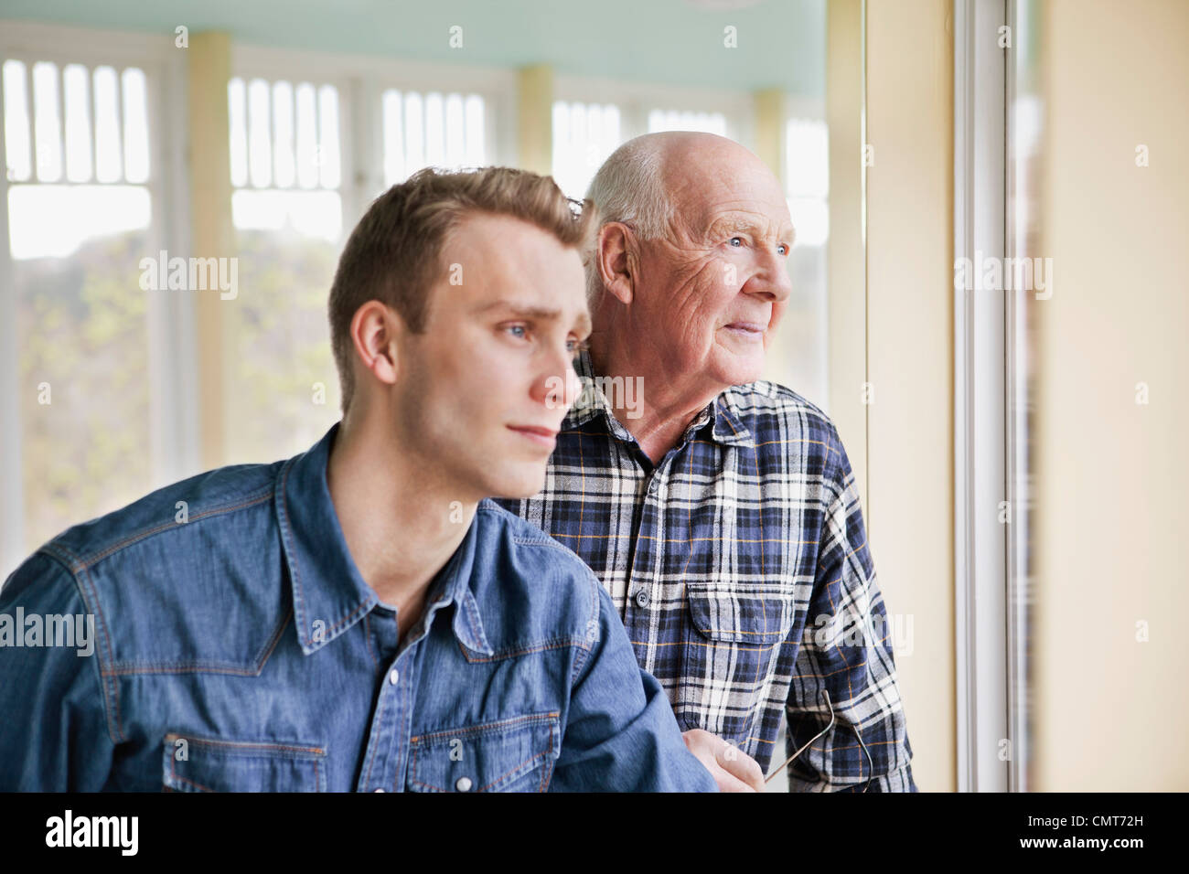 Elderly and younger man looking out through window Stock Photo - Alamy