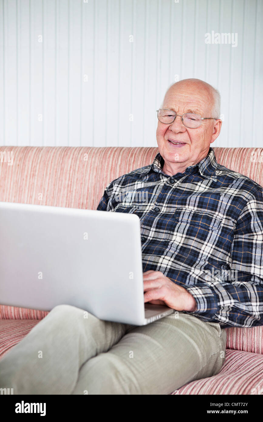 Elderly man sitting on sofa with laptop Stock Photo - Alamy