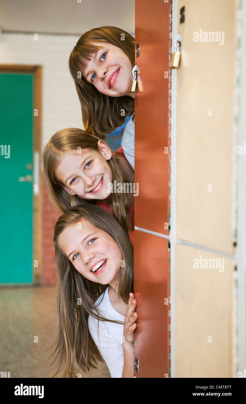 Three girls (12-13) hiding behind a locker Stock Photo - Alamy