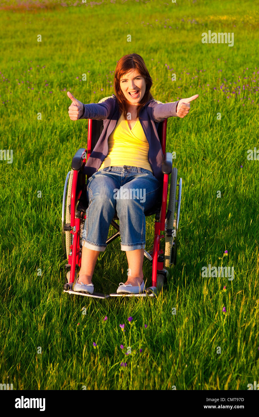 Happy handicapped woman with thumbs up seated on a wheelchair over a ...