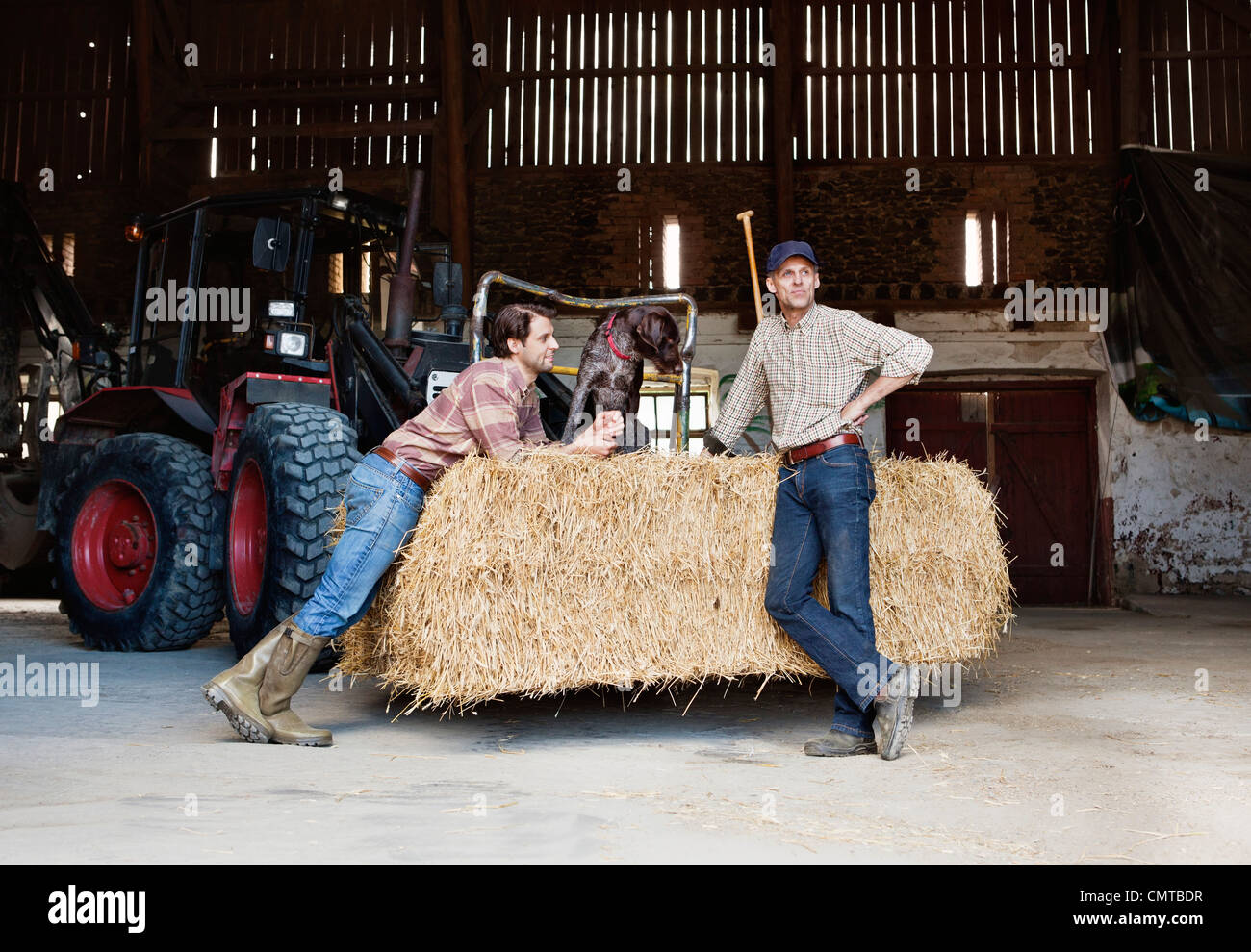 Men leaning on hay with tractor in background Stock Photo - Alamy