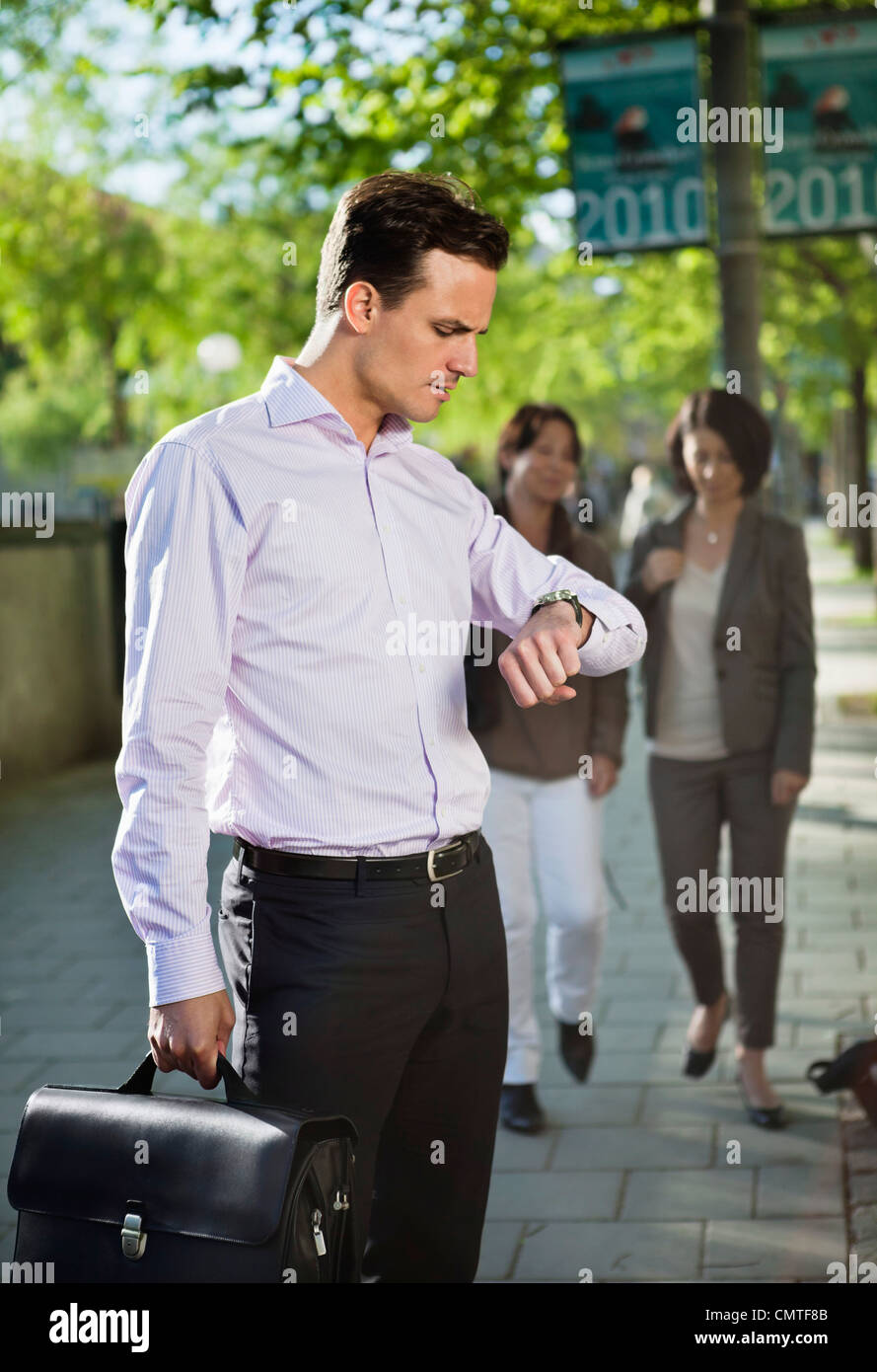 Man looking at watch with people in the background Stock Photo - Alamy