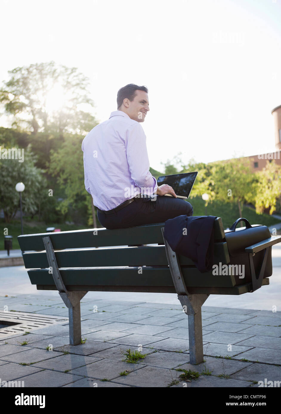 Smiling businessman sitting on bench and using laptop Stock Photo - Alamy