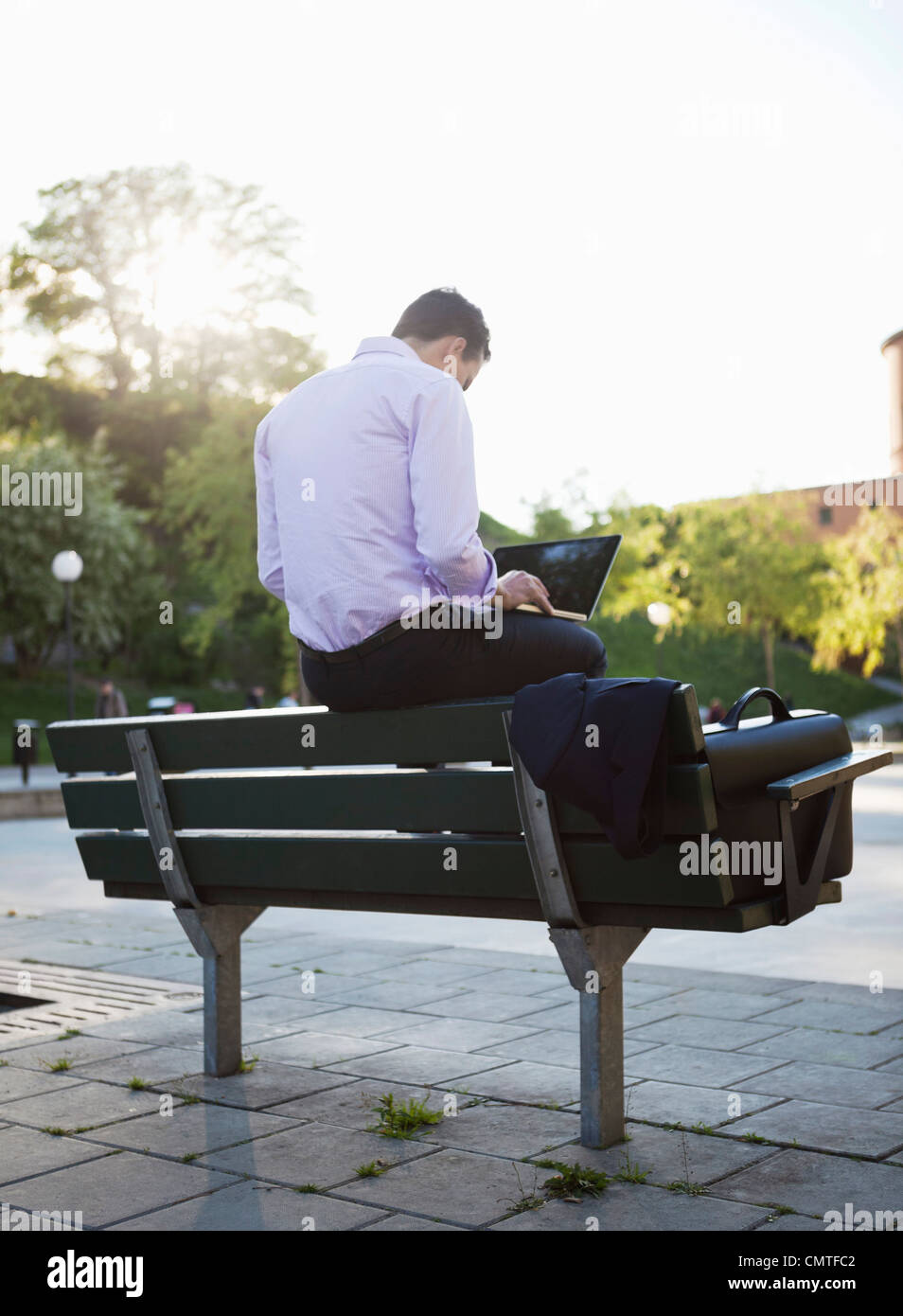 Rear view of man sitting on bench and using laptop Stock Photo - Alamy