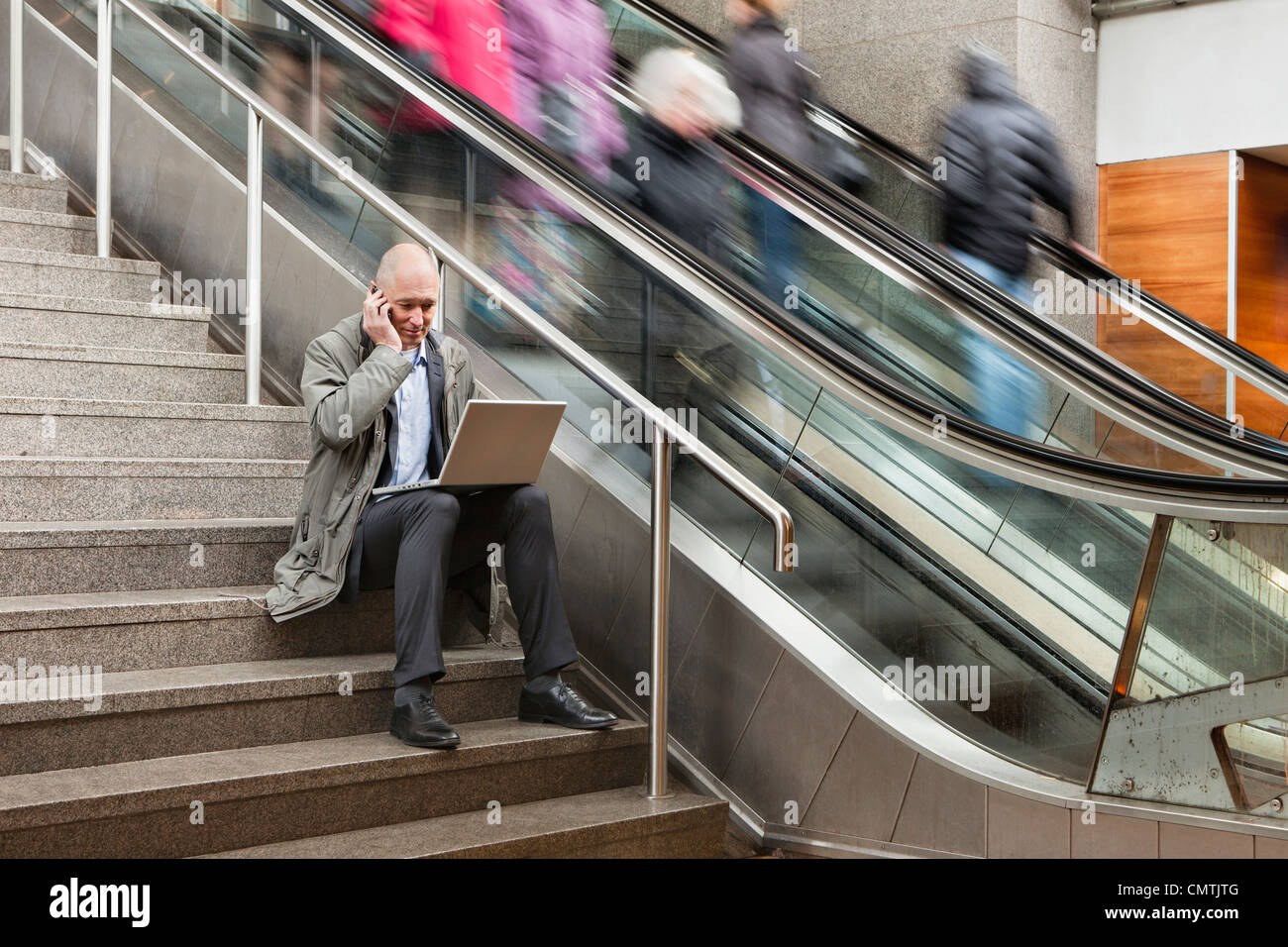 Man in stairs using laptop and cell phone Stock Photo - Alamy