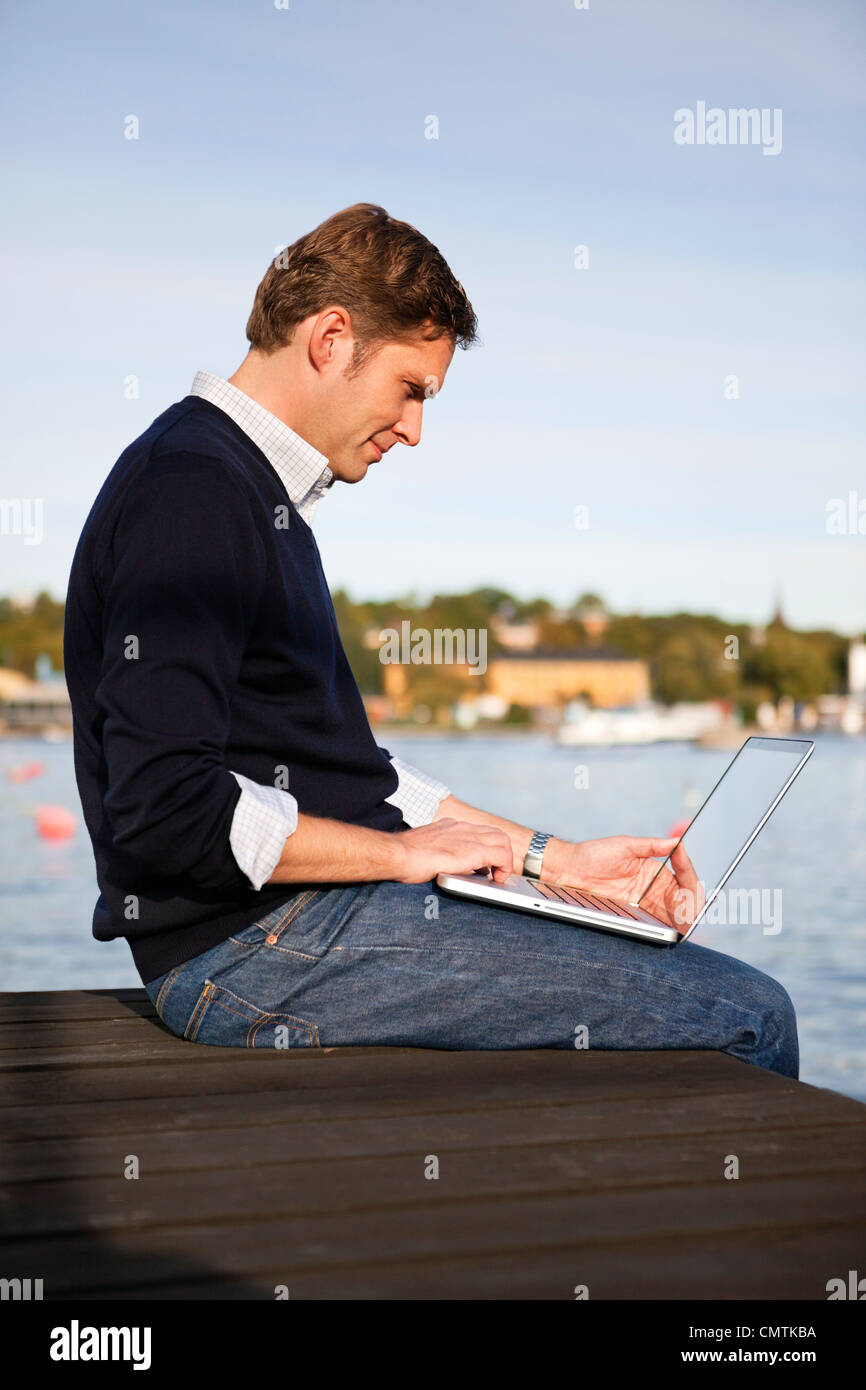 Concentrated man using laptop while sitting on jetty Stock Photo - Alamy