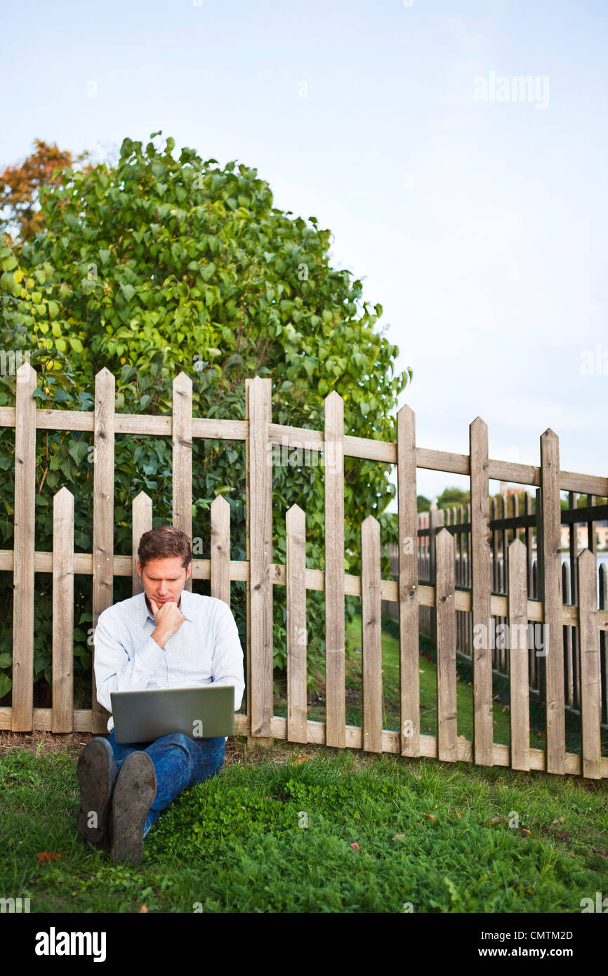 Man leaning against fence with computer on his lap Stock Photo - Alamy