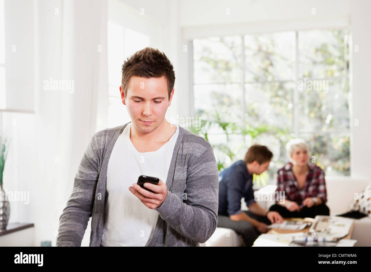 Man looking at mobile phone with friends in the background Stock Photo ...