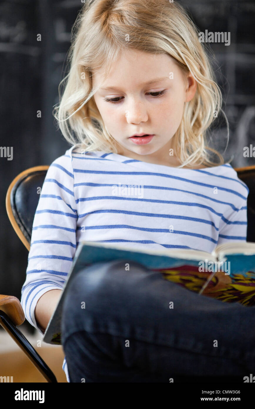 Girl reading book on chair Stock Photo - Alamy