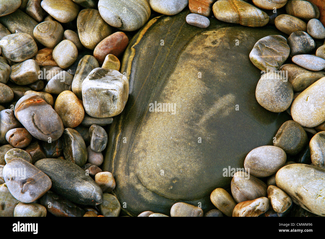 Water worn pebbles on the beach surrounding a larger rock Stock Photo ...