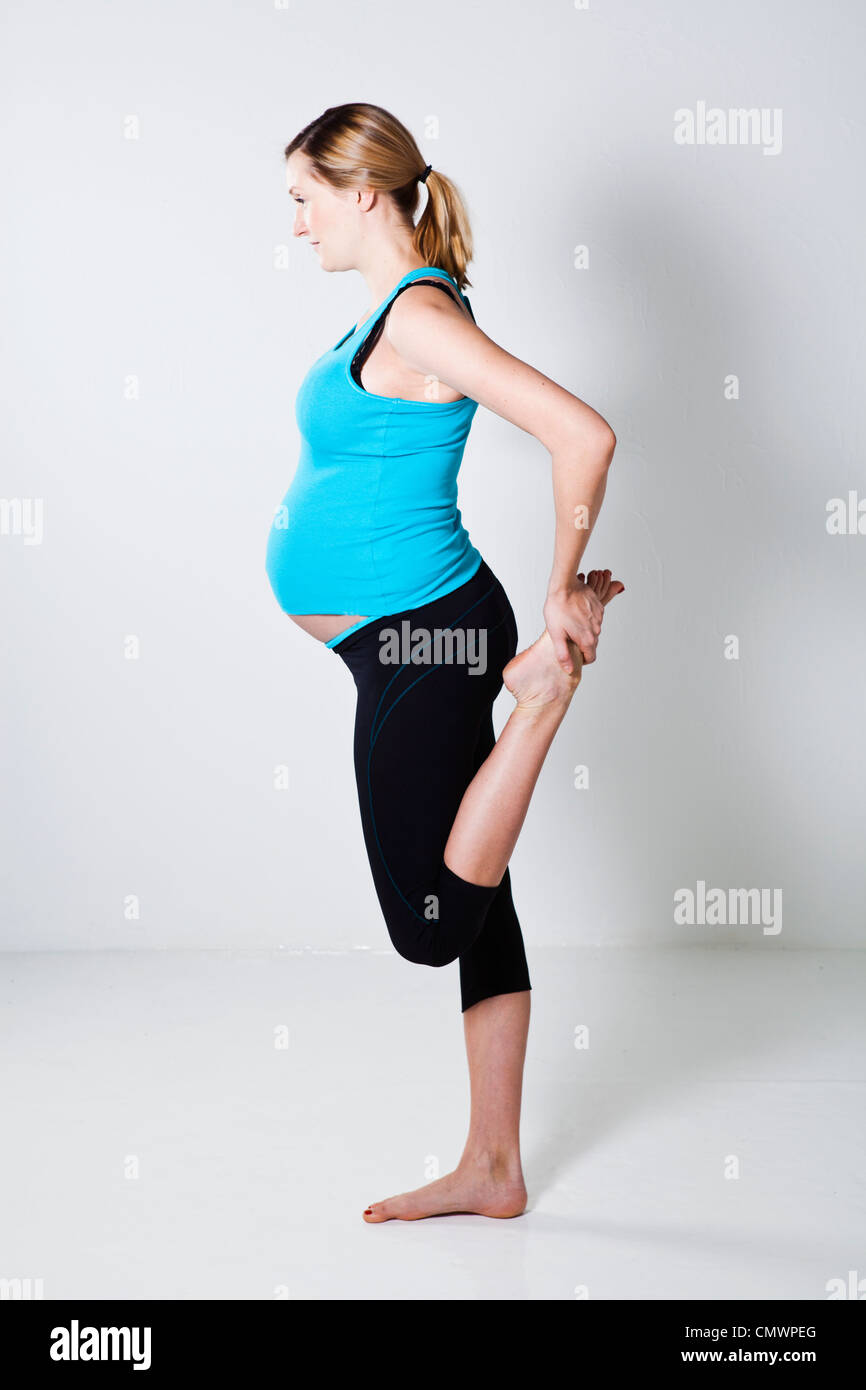 Pregnant woman performing a leg stretching exercise for the front thigh ...