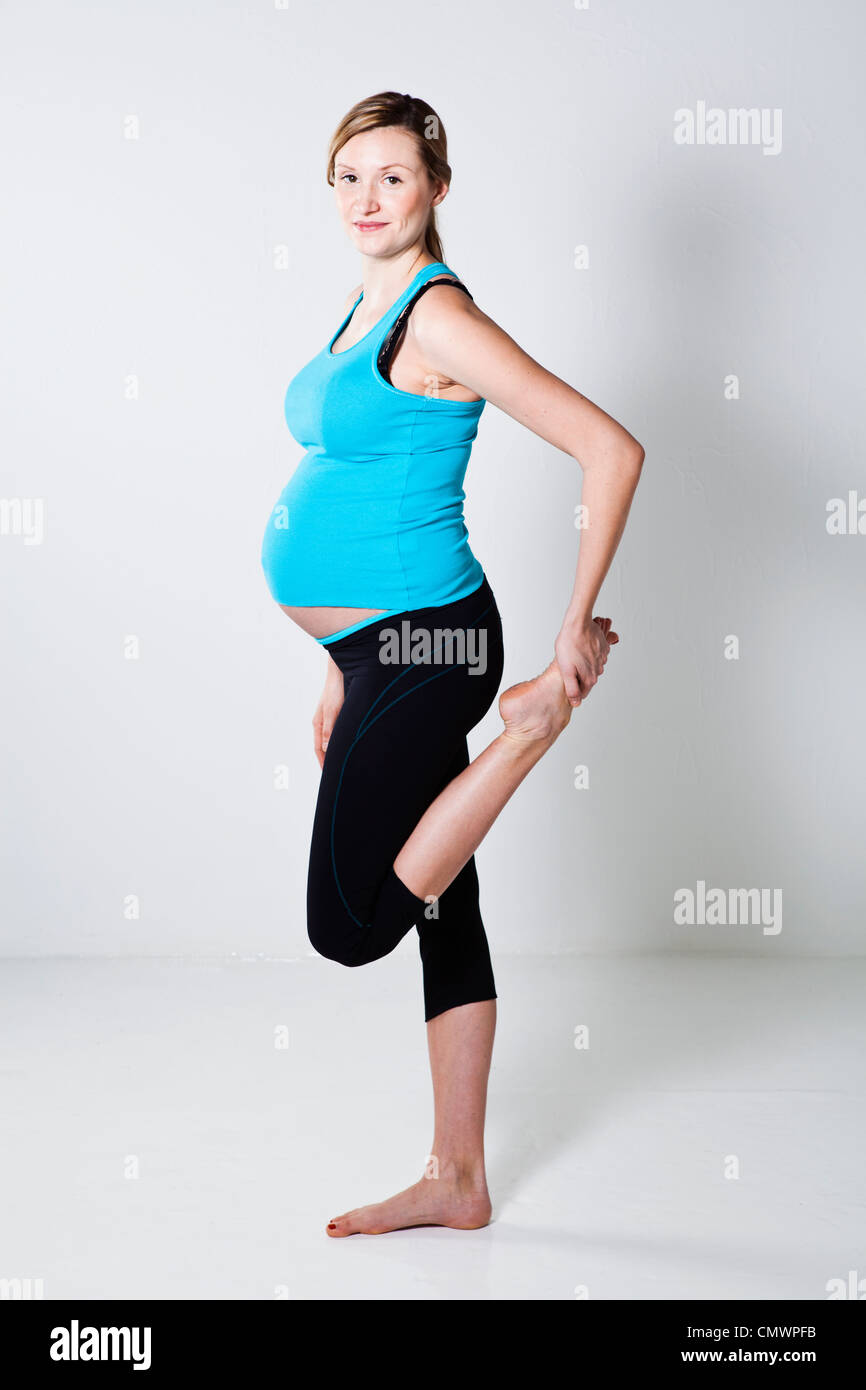 Pregnant woman performing a leg stretching exercise for the front thigh ...