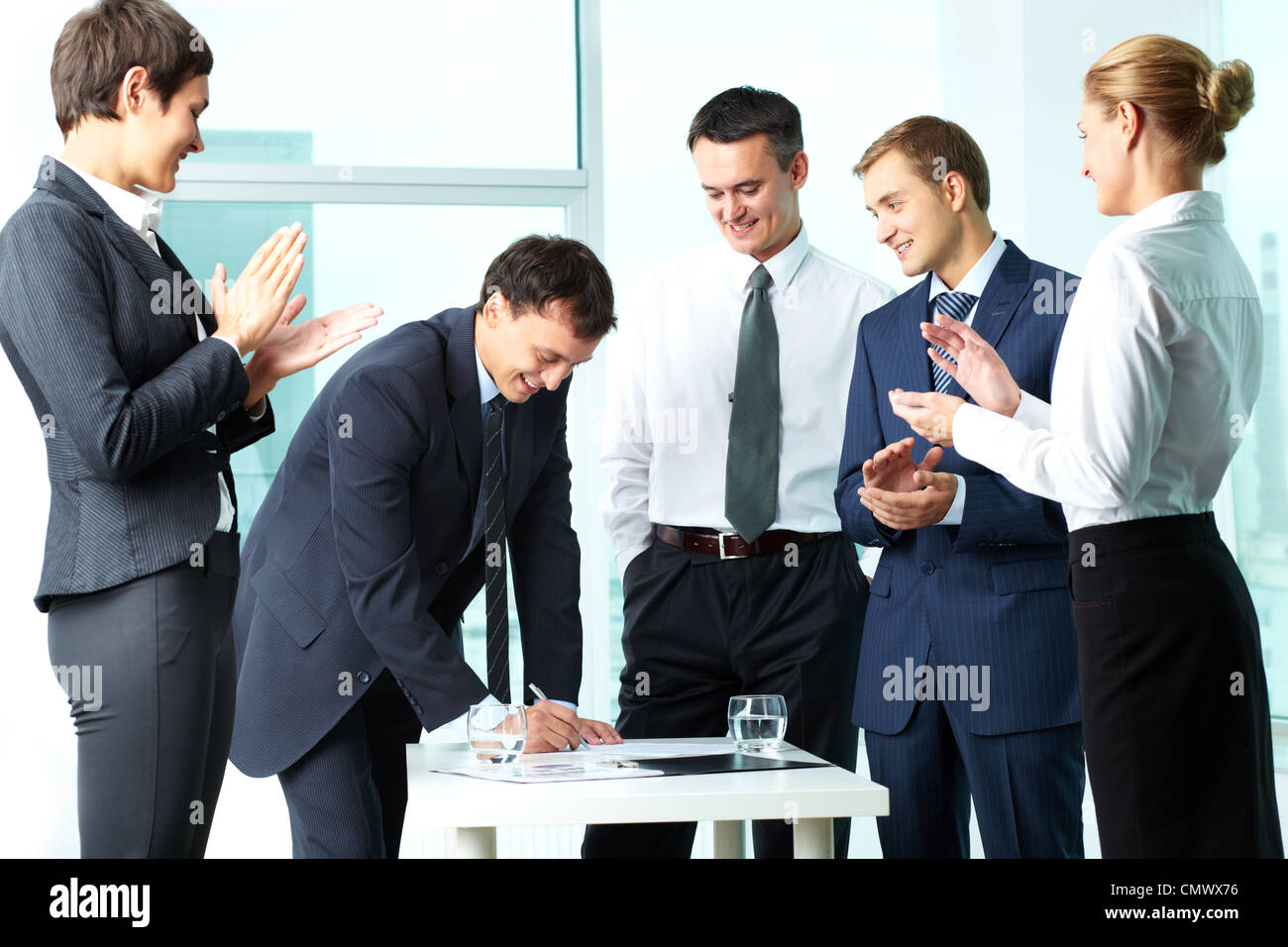 Image of co-workers congratulating their colleague while he signing ...